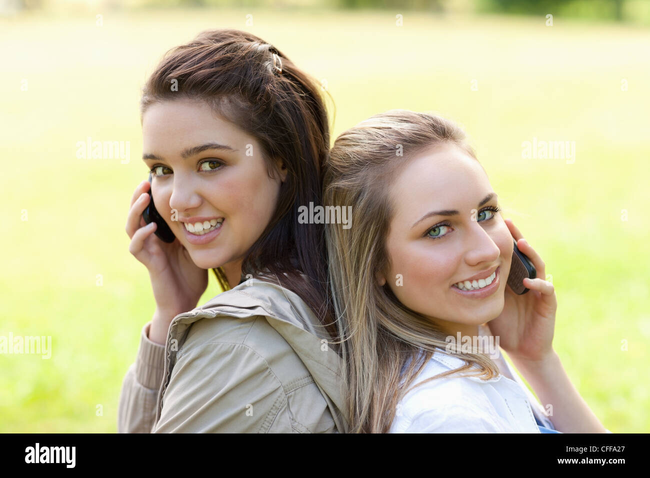 Young friends standing back to back while talking on the phone Stock ...