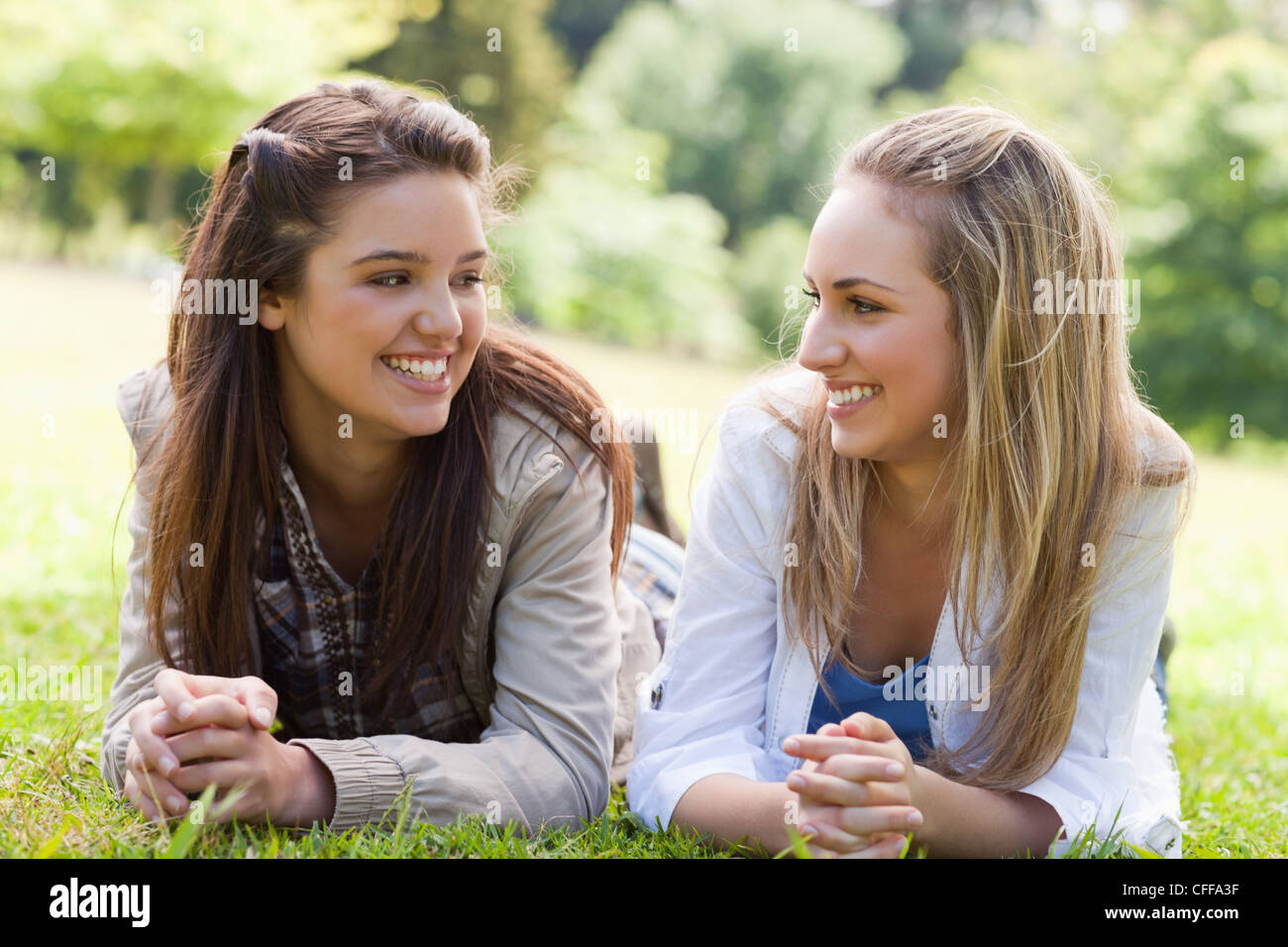 Young smiling girls looking at each other while lying on the grass ...