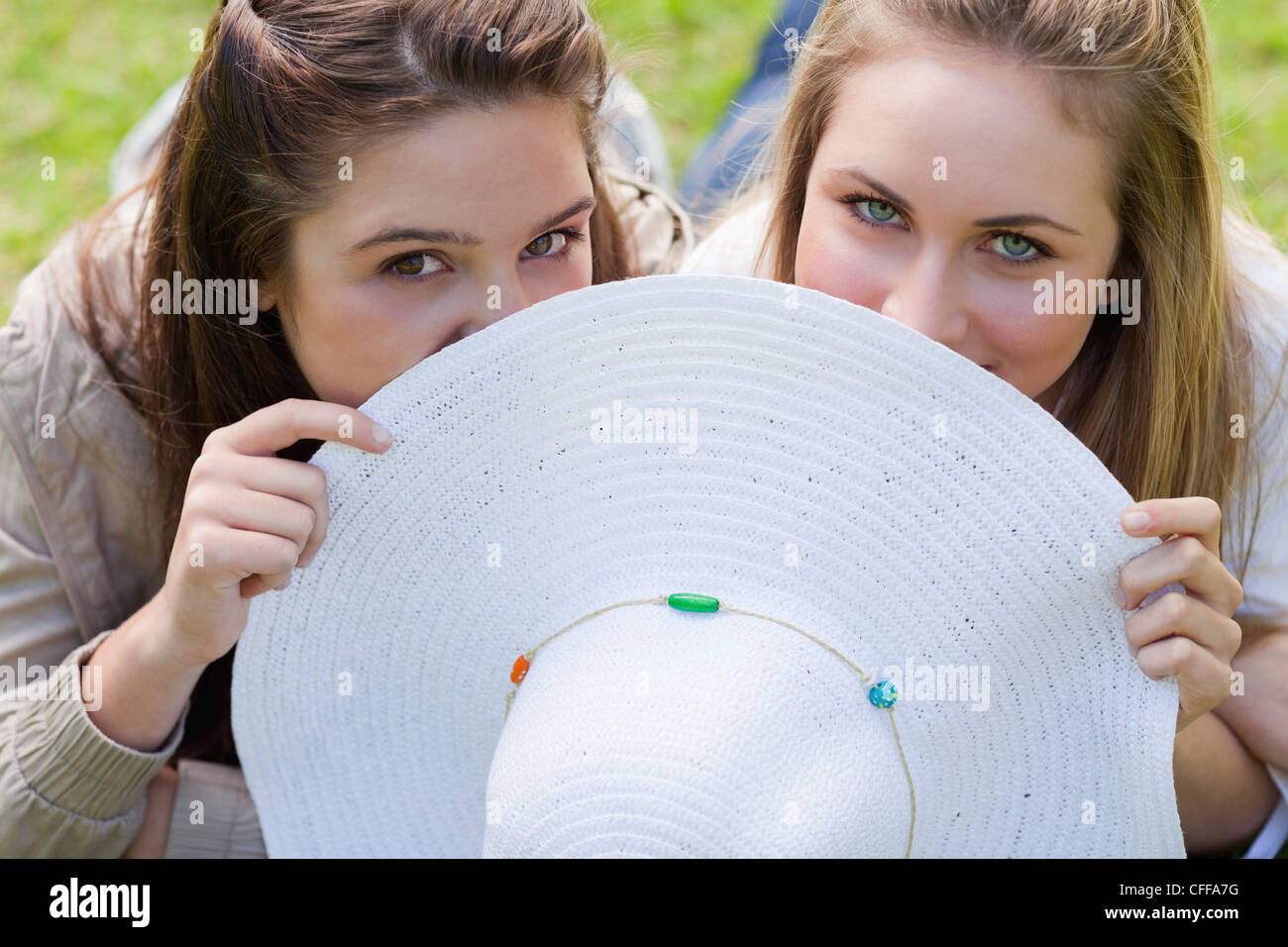 Young friends hiding their faces behind a white hat Stock Photo - Alamy