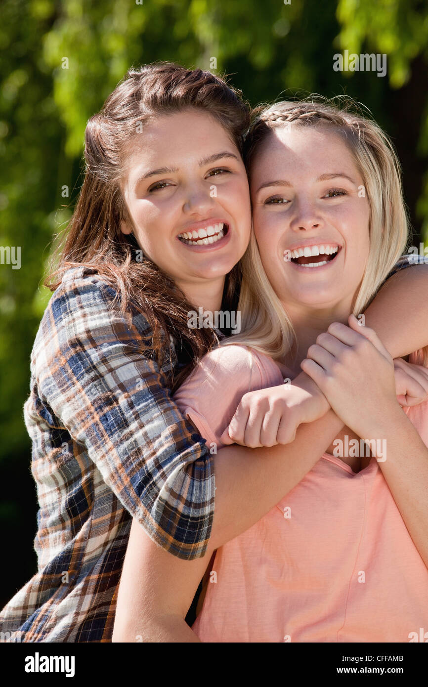 Young smiling girl hugging her friend with her arms wrapped around her ...