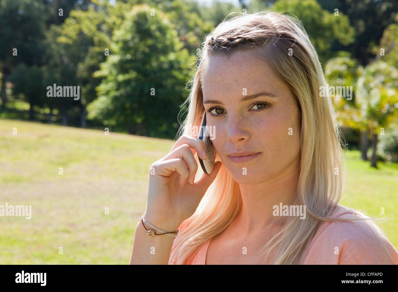 Young serious girl standing upright in a park while using her cellphone ...