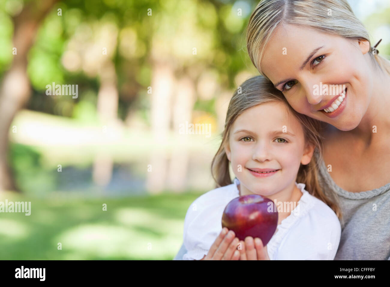 A smiling mother with her daughter who is holding a red apple Stock ...