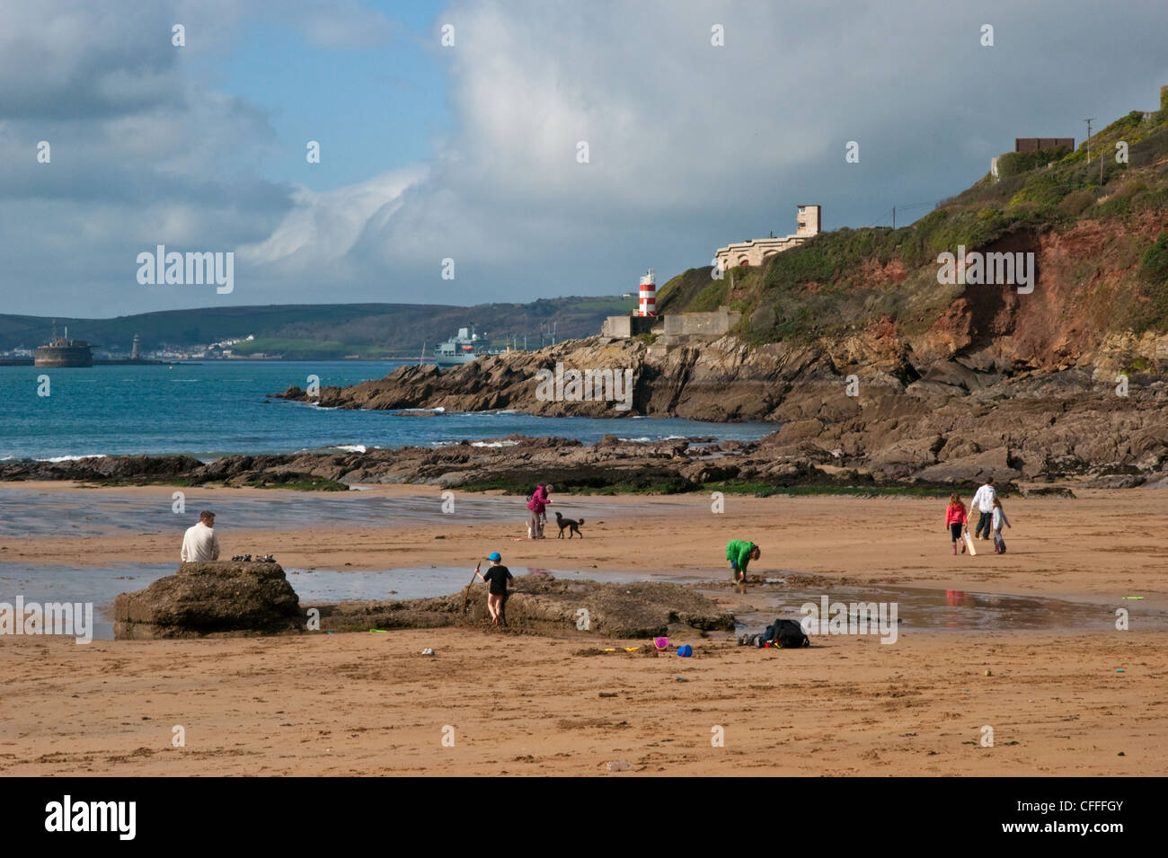 A sandy beach with the tide out and cliffs and a fort in the background ...