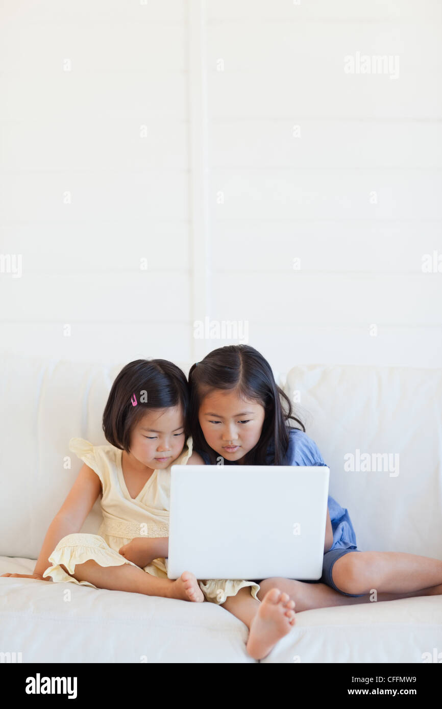 Both sisters watch the laptop screen intently while sitting on the ...
