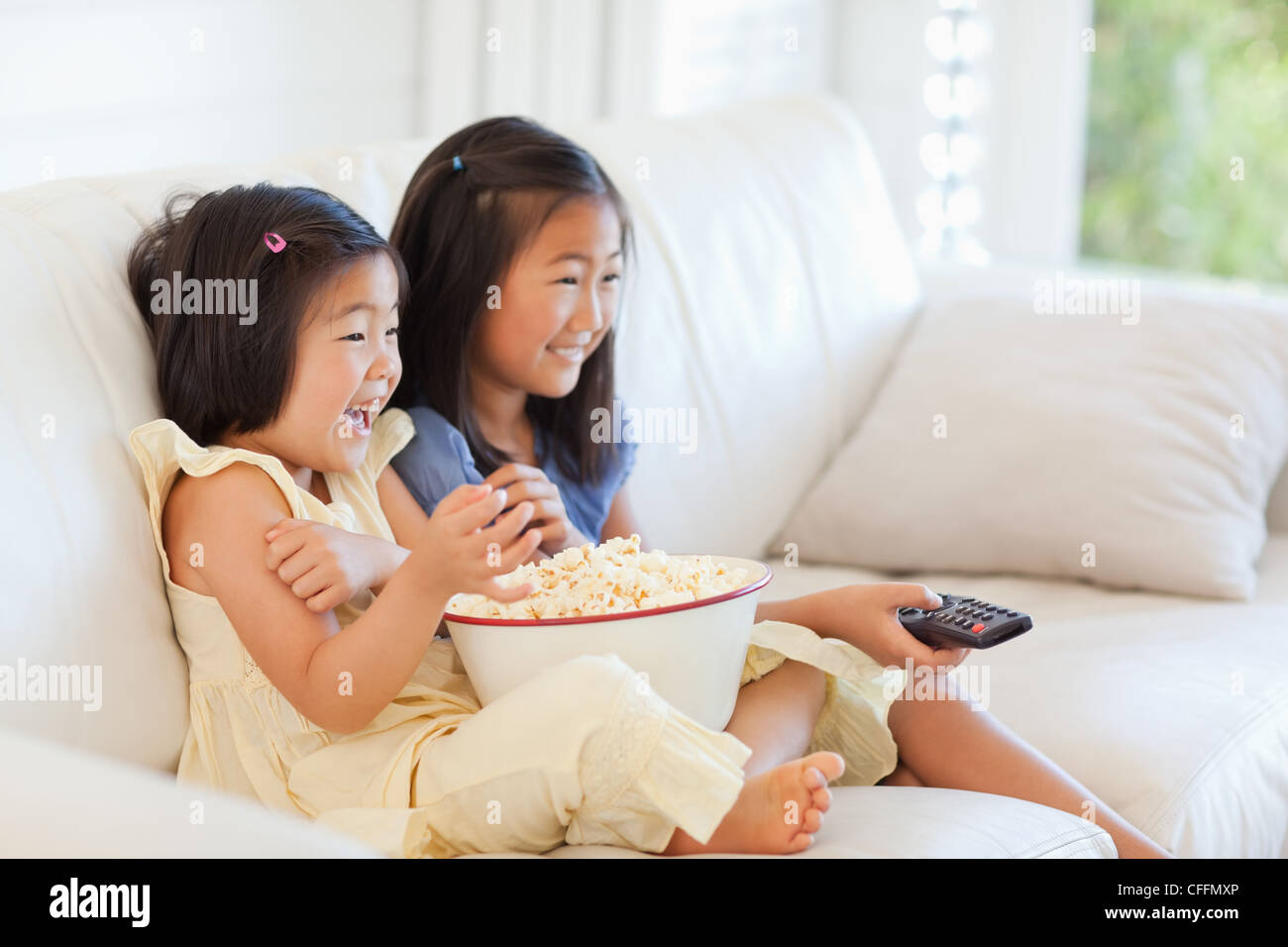Side view of two sisters watching tv and eating popcorn Stock Photo - Alamy