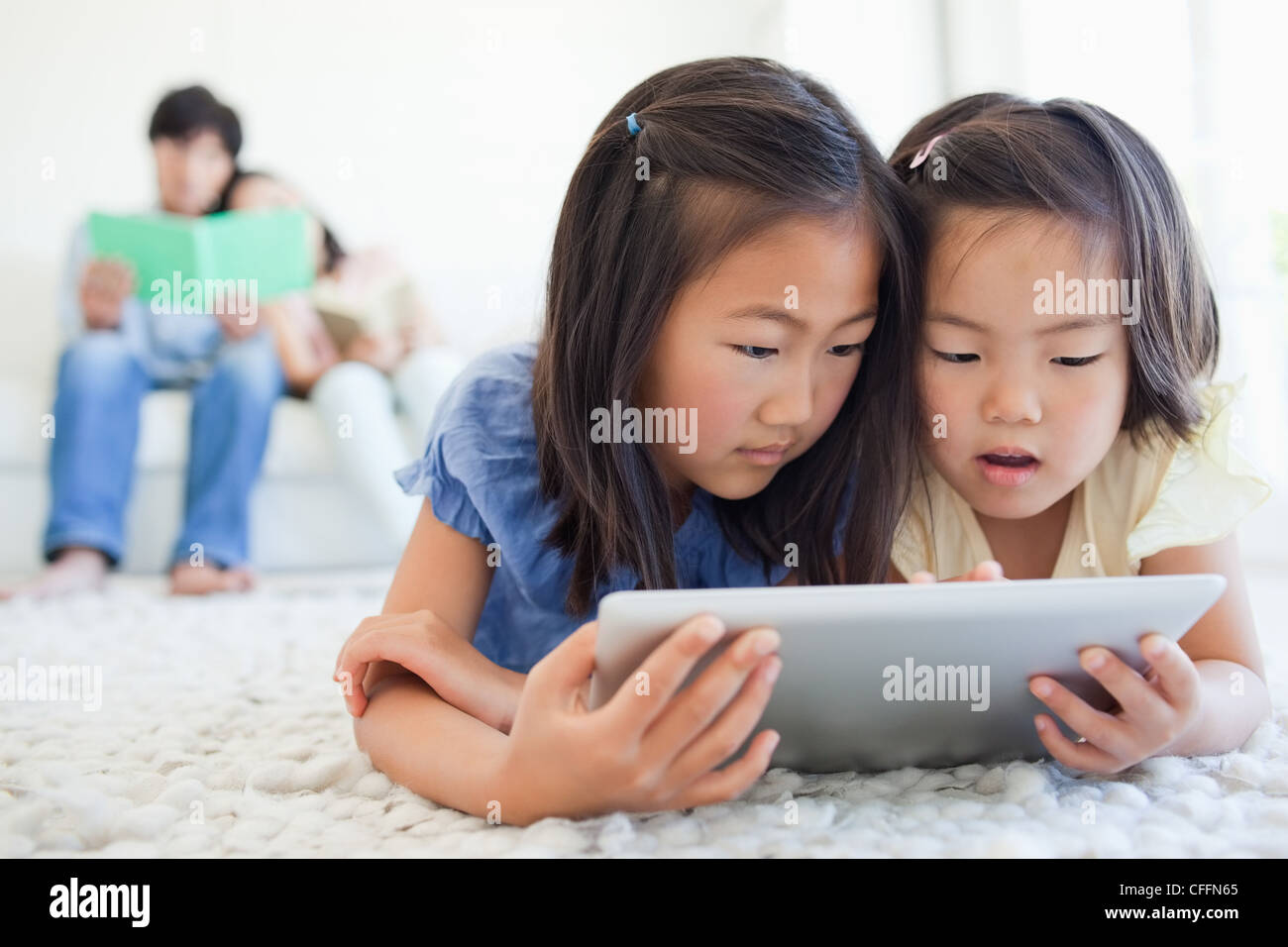 The parents read a book on the couch as the kids use the tablet Stock ...