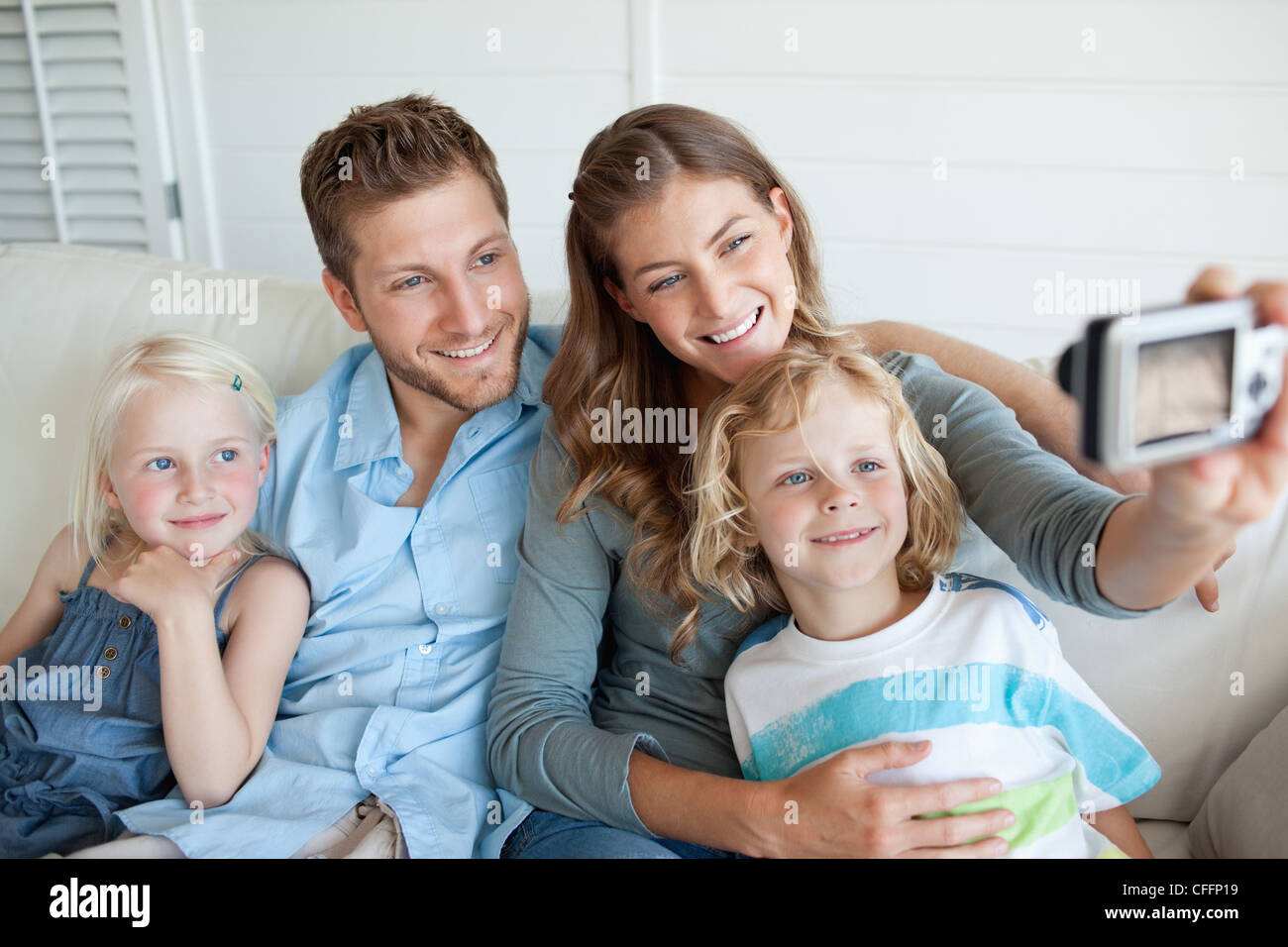The family smiles and sit on the couch as they pose for a family photo ...