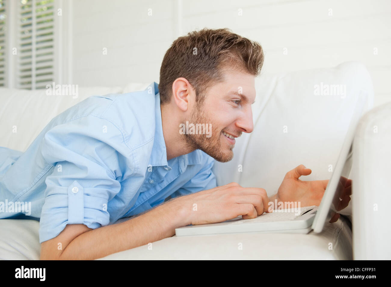 Side view of a man using his laptop while lying across his couch Stock ...