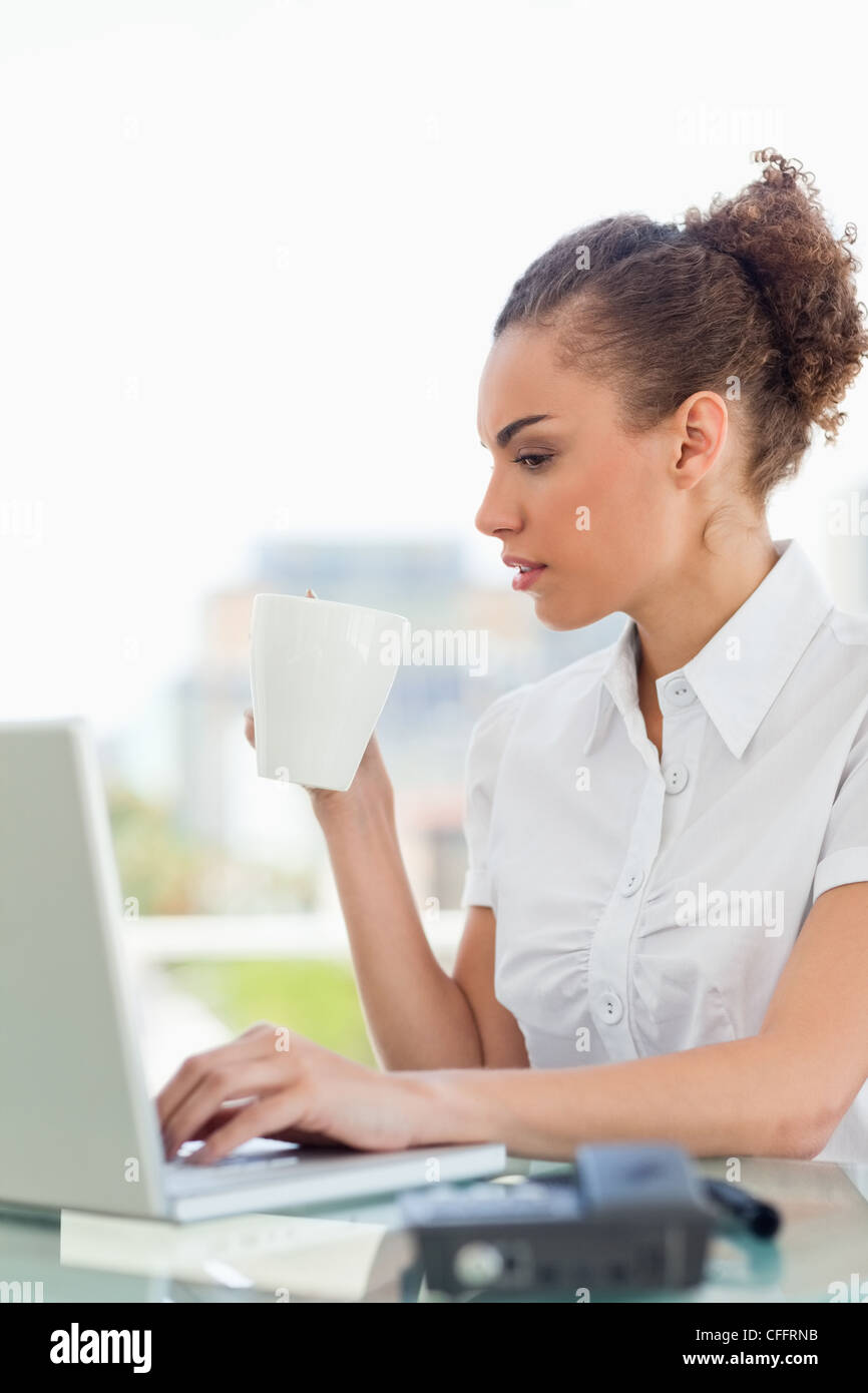 Frizzy woman tapping on her laptop while drinking a coffee Stock Photo ...