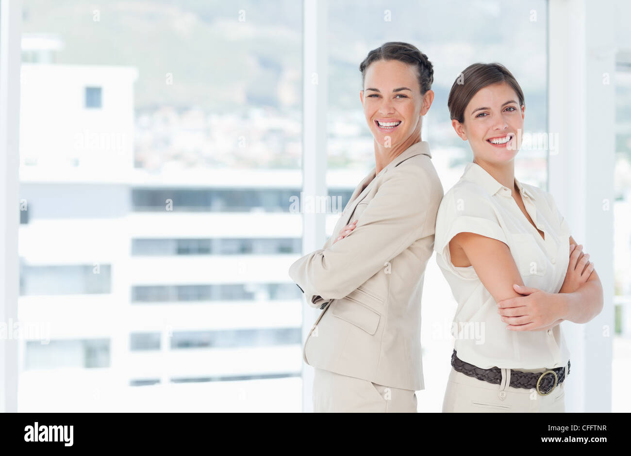 Two business women back to back smiling Stock Photo - Alamy