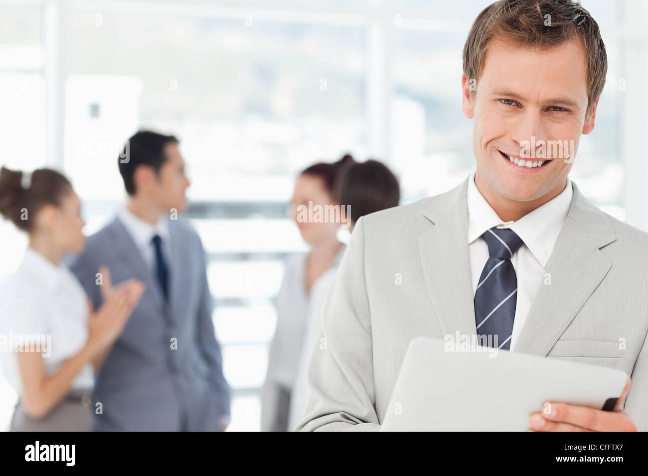 Smiling salesman with his tablet computer and colleagues behind him ...