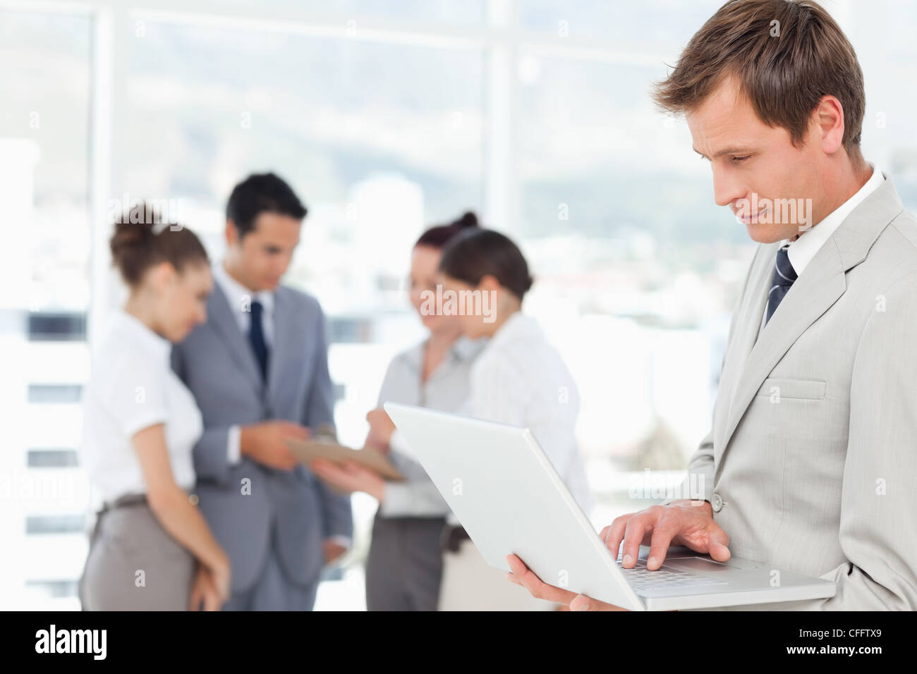 Salesman working on his laptop with colleagues behind him Stock Photo ...