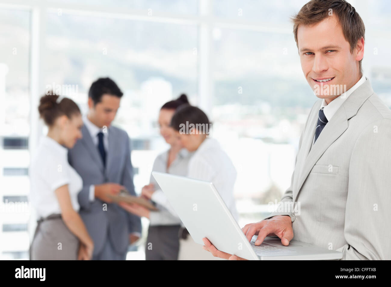 Smiling salesman with his laptop and colleagues behind him Stock Photo ...