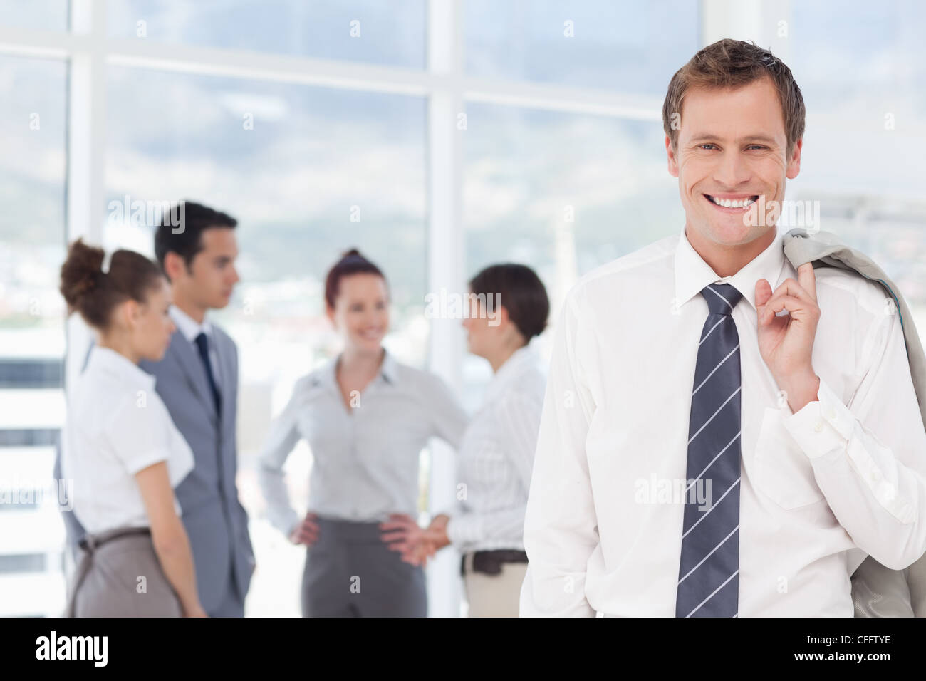 Smiling salesman with jacket over his shoulder and colleagues behind ...