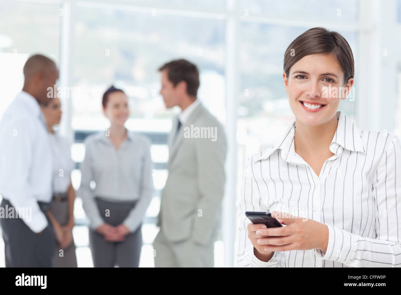 Smiling saleswoman with cellphone and associates behind her Stock Photo ...