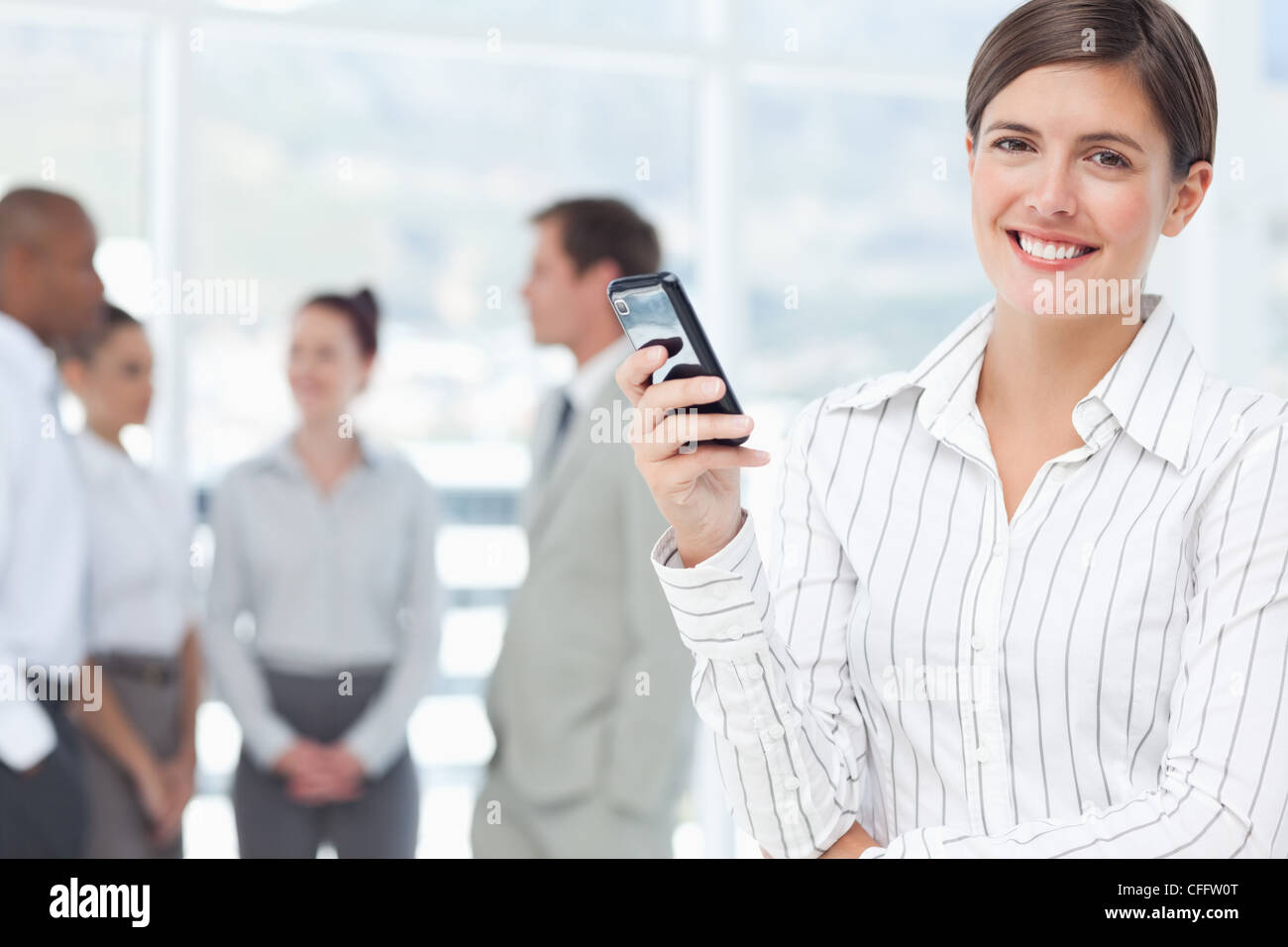 Smiling saleswoman with mobile phone and colleagues behind her Stock ...