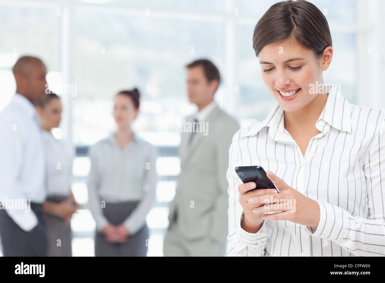 Smiling saleswoman writing text message with colleagues behind her ...