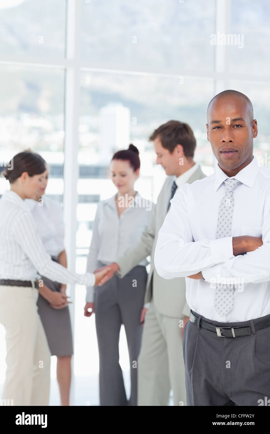 Confident salesman with his arms crossed and colleagues behind him ...