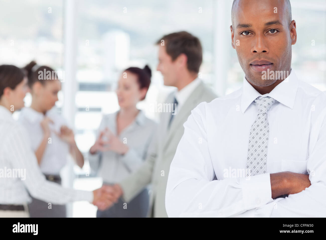 Confident salesman with his arms folded and colleagues behind him Stock ...