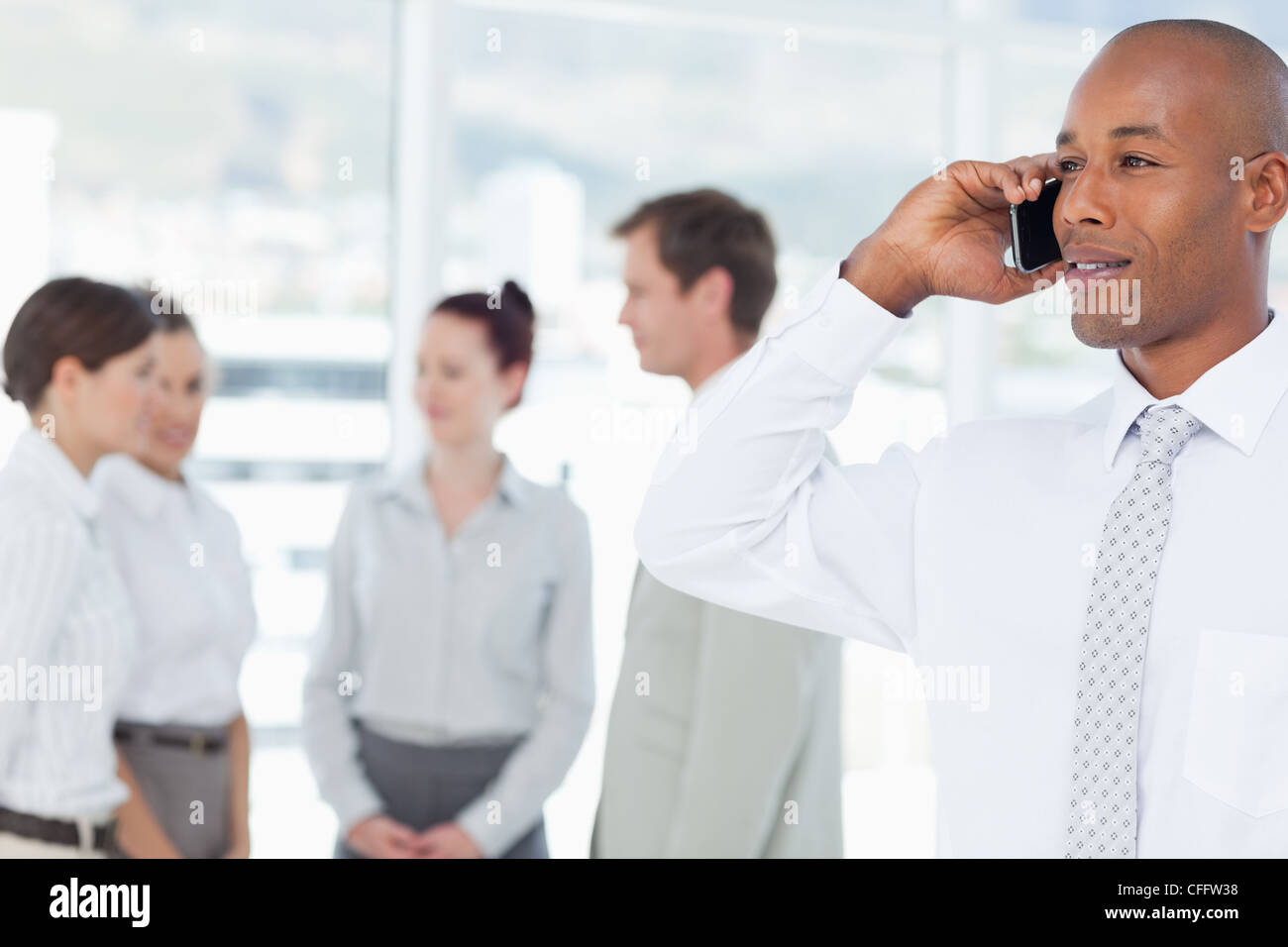 Salesman on his cellphone with associates behind him Stock Photo - Alamy