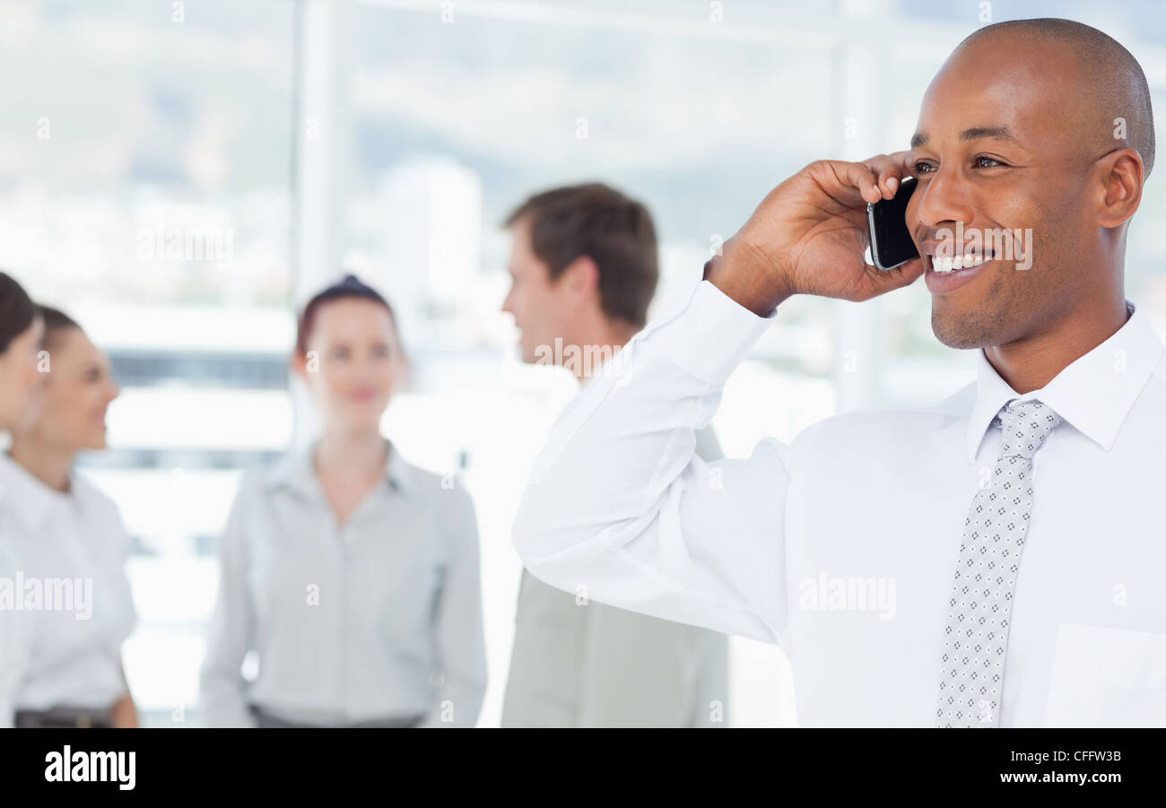 Smiling salesman on his cellphone with associates behind him Stock ...
