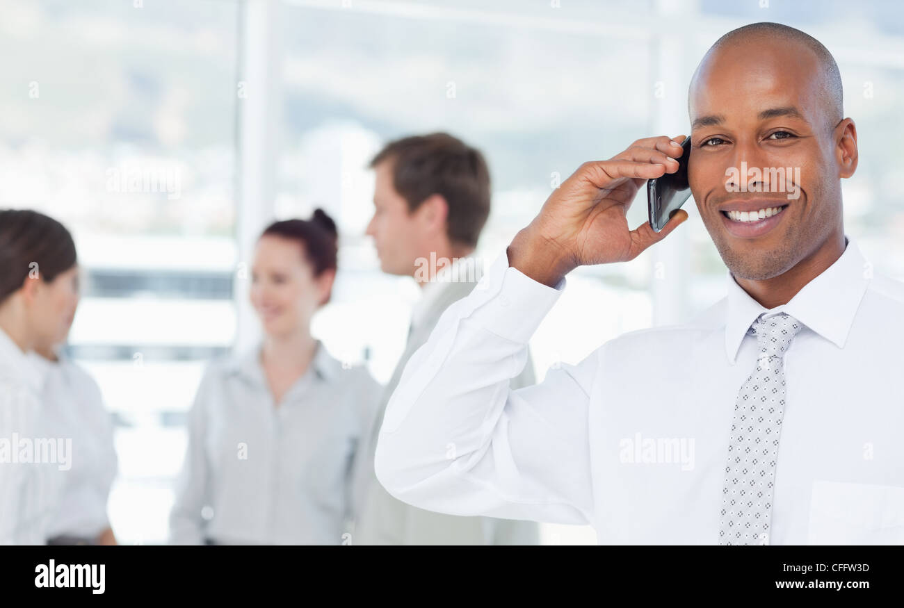 Smiling salesman on his mobile phone with colleagues behind him Stock ...