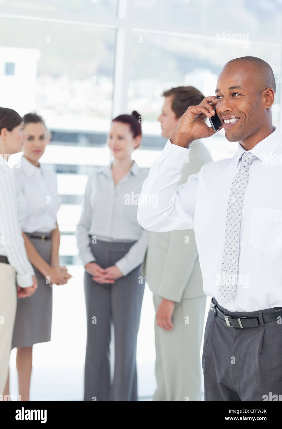 Smiling salesman on his cellphone and colleagues behind him Stock Photo ...