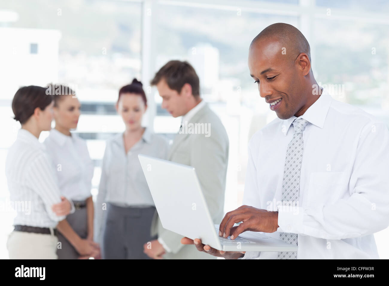 Smiling salesman using laptop with colleagues behind him Stock Photo ...