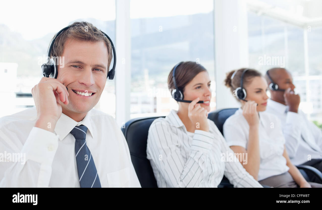 Smiling telephone help desk employee sitting next to his colleagues ...