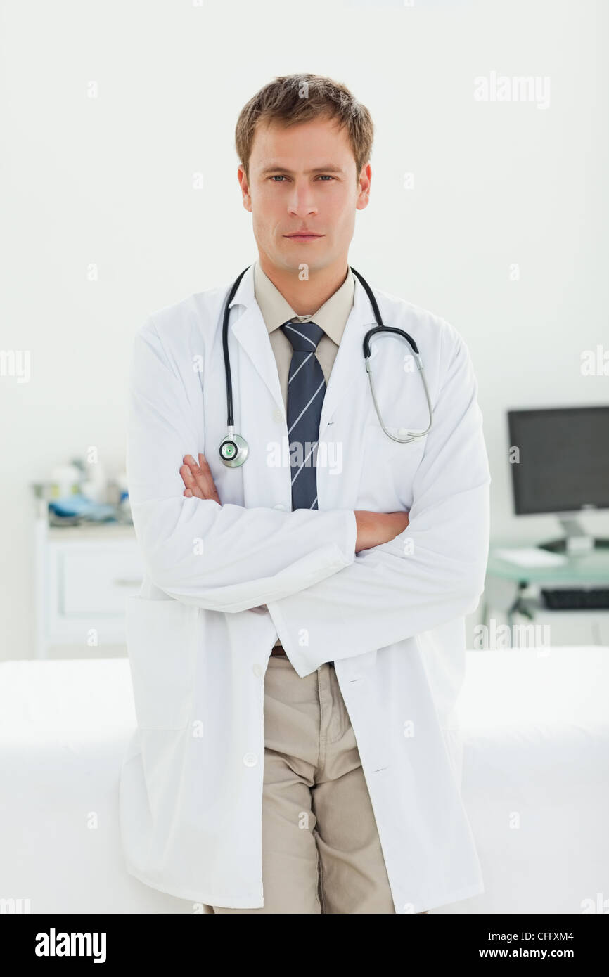 Serious doctor with arms folded standing in his examination room Stock ...