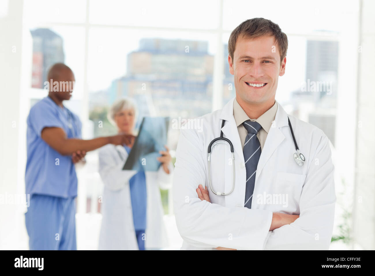 Doctor with his arms folded and colleagues behind him Stock Photo - Alamy