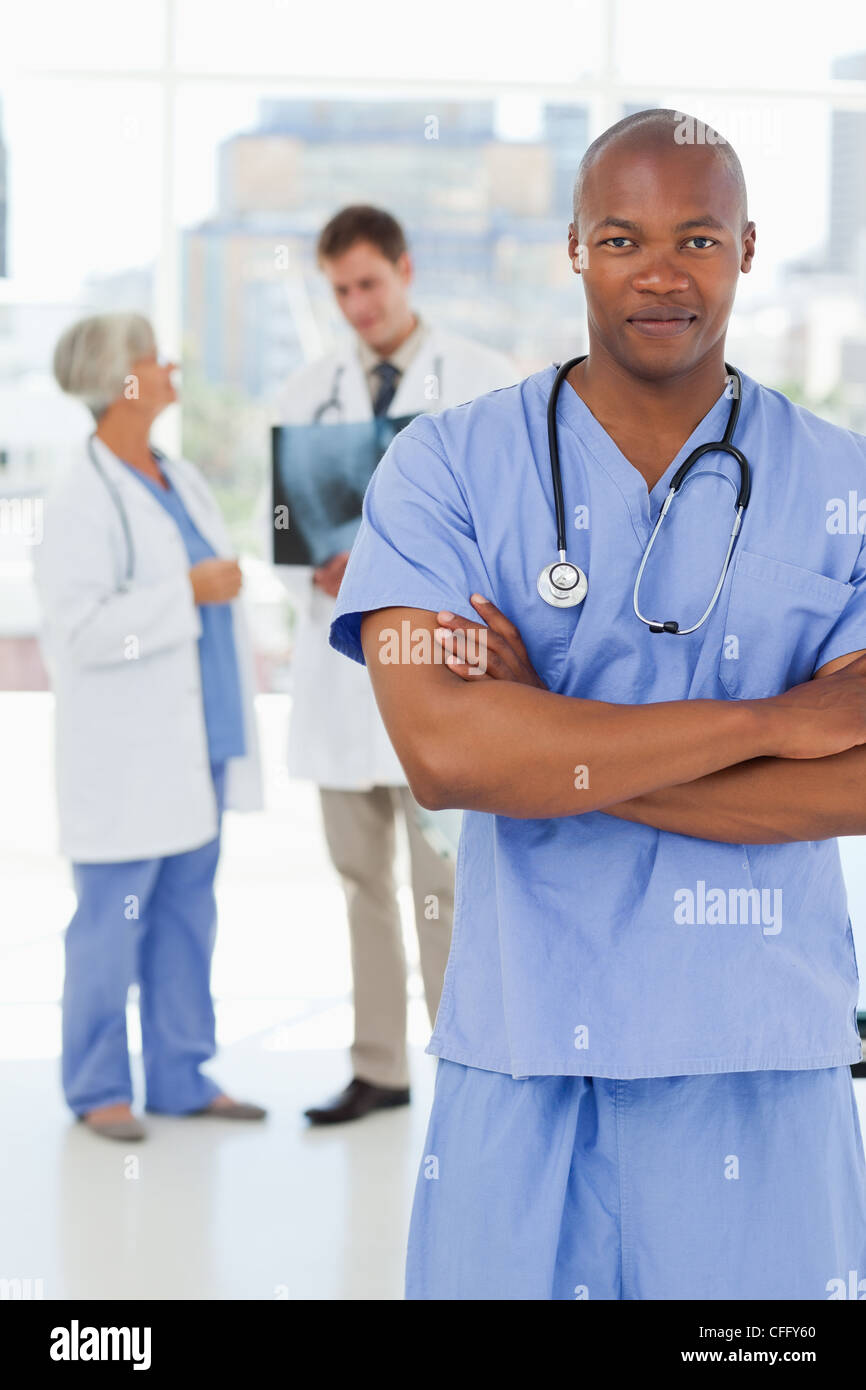 Doctor in scrubs with folded arms and colleagues behind him Stock Photo ...