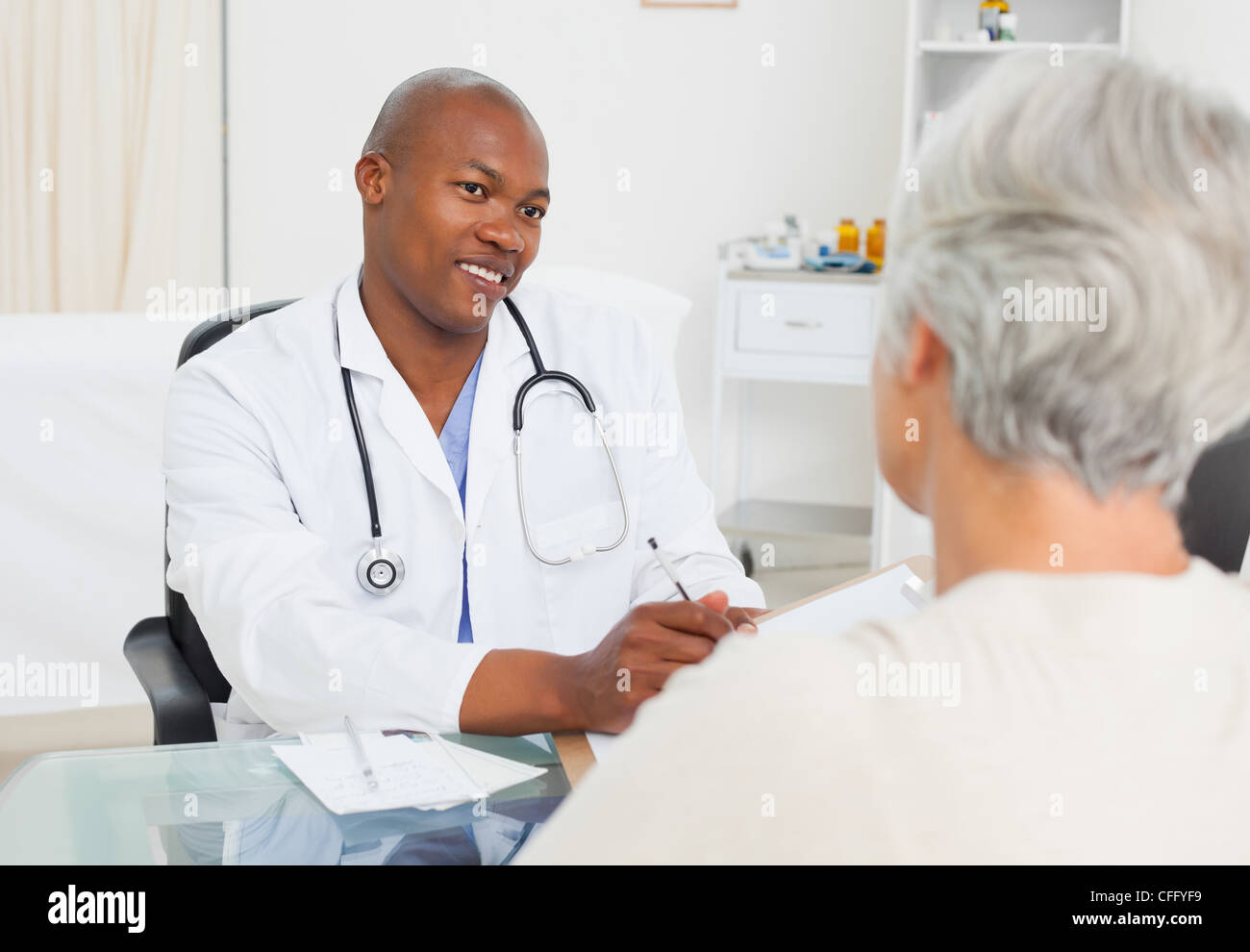 Smiling doctor is taking notes while his patient is talking Stock Photo ...