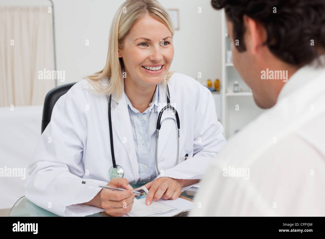 Smiling doctor taking notes while listening to patient Stock Photo - Alamy