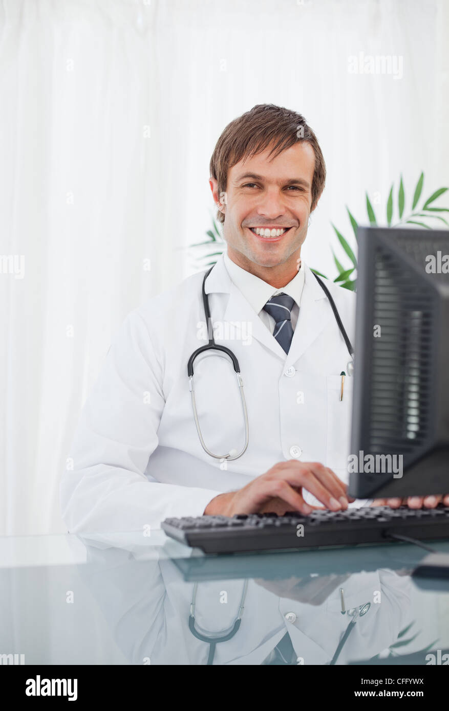 Smiling doctor working on his computer while sitting at a desk Stock ...