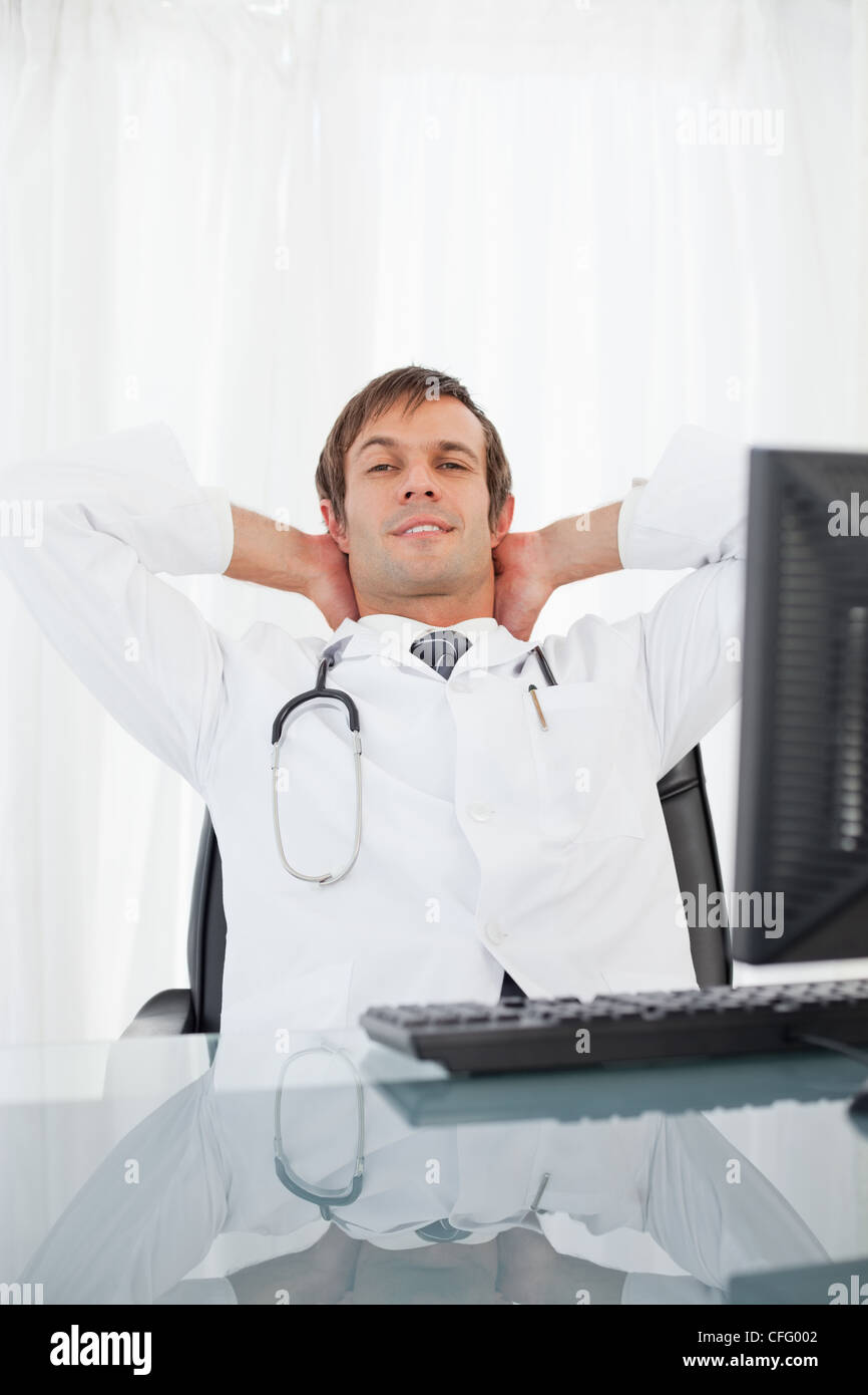 Relaxed surgeon sitting at the desk with his hands behind his neck ...
