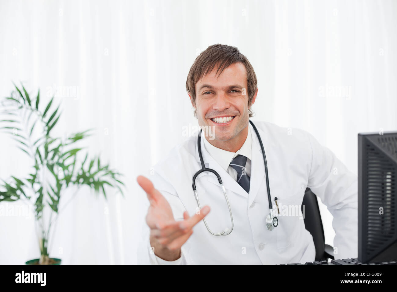 Smiling doctor extending his hand while sitting at the desk Stock Photo ...