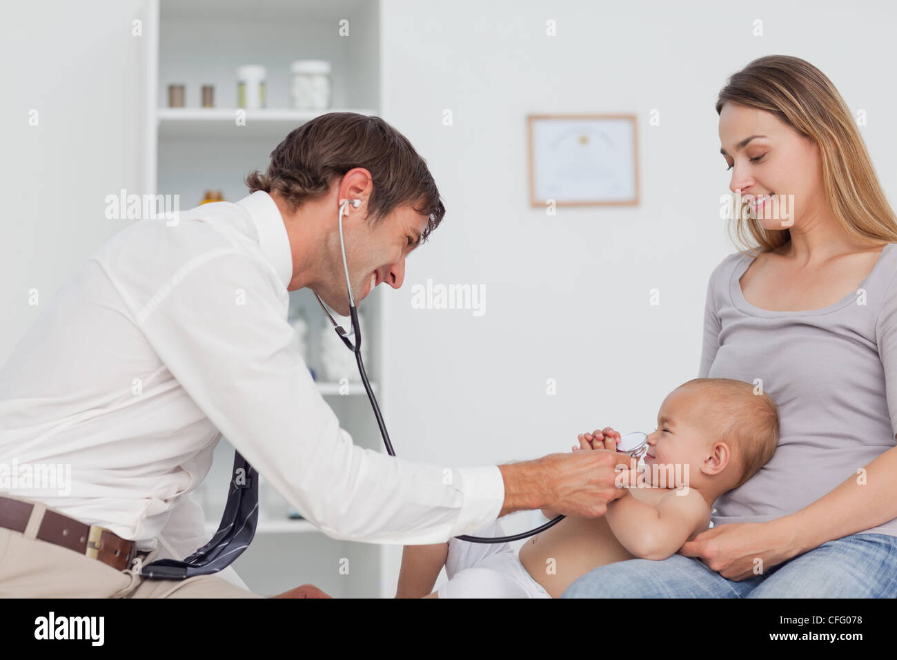Smiling doctor examining a crying little baby being held by her mother ...