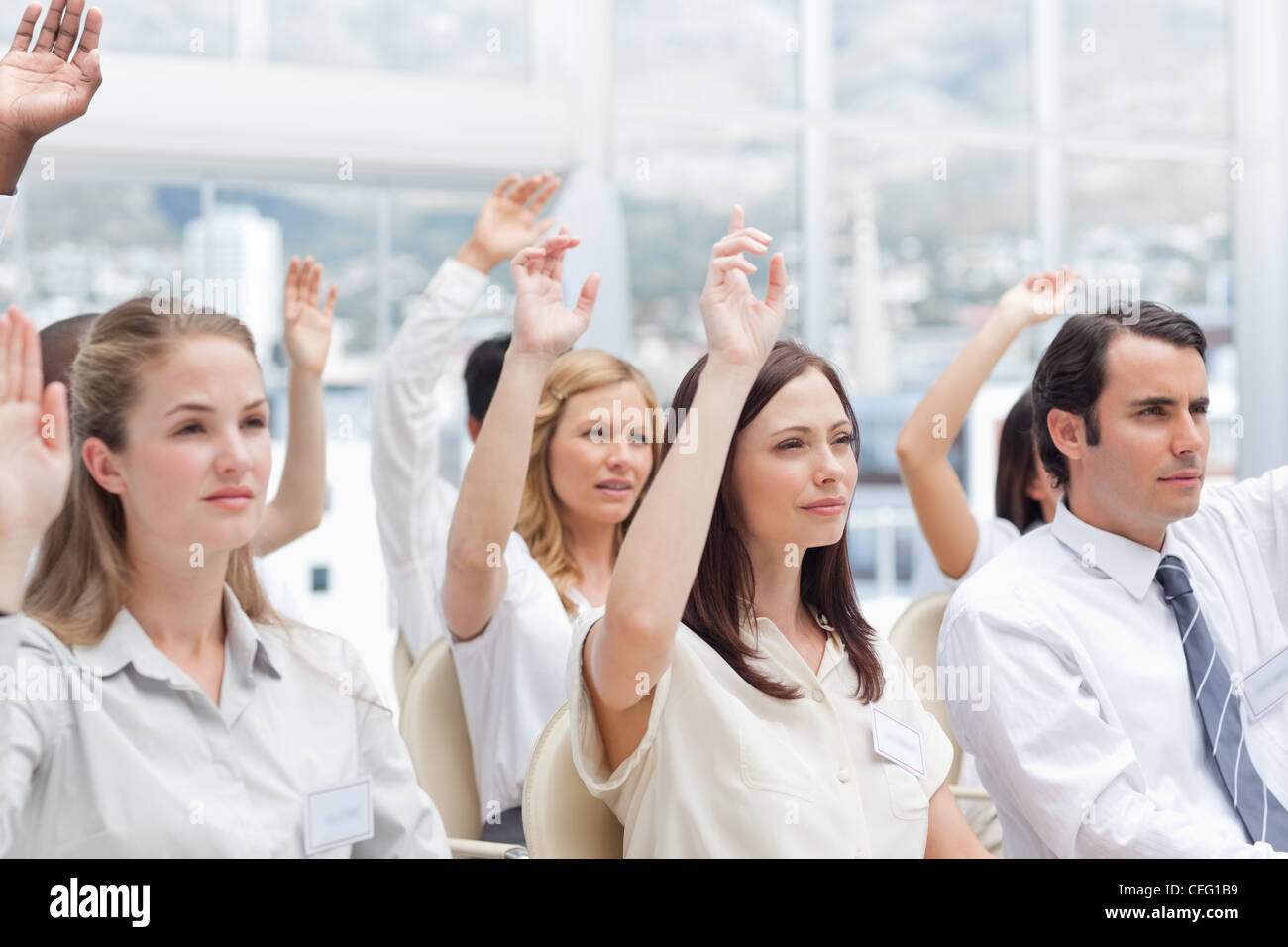 Serious colleagues raising their hands as they sit together Stock Photo ...
