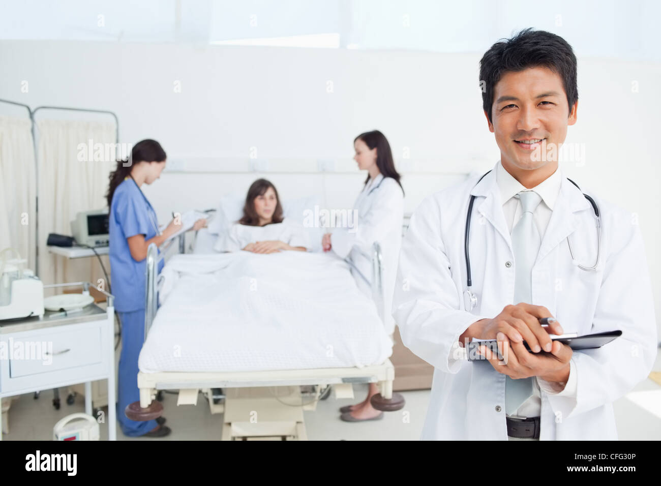 Doctor holding a clipboard while his colleagues are treating a patient ...