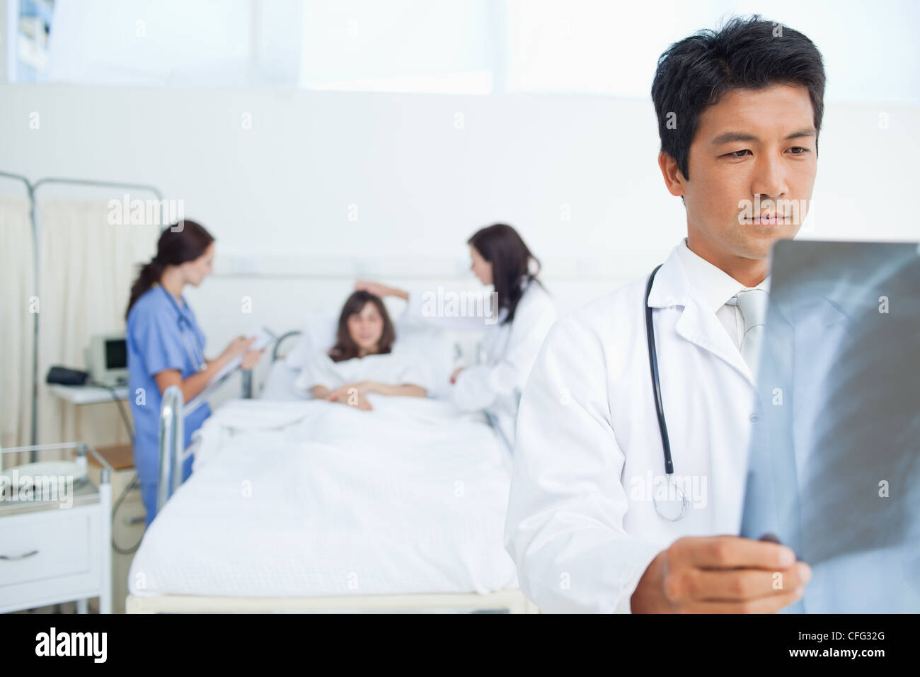 Doctor looking at an x-ray scan while his colleagues treat a patient ...