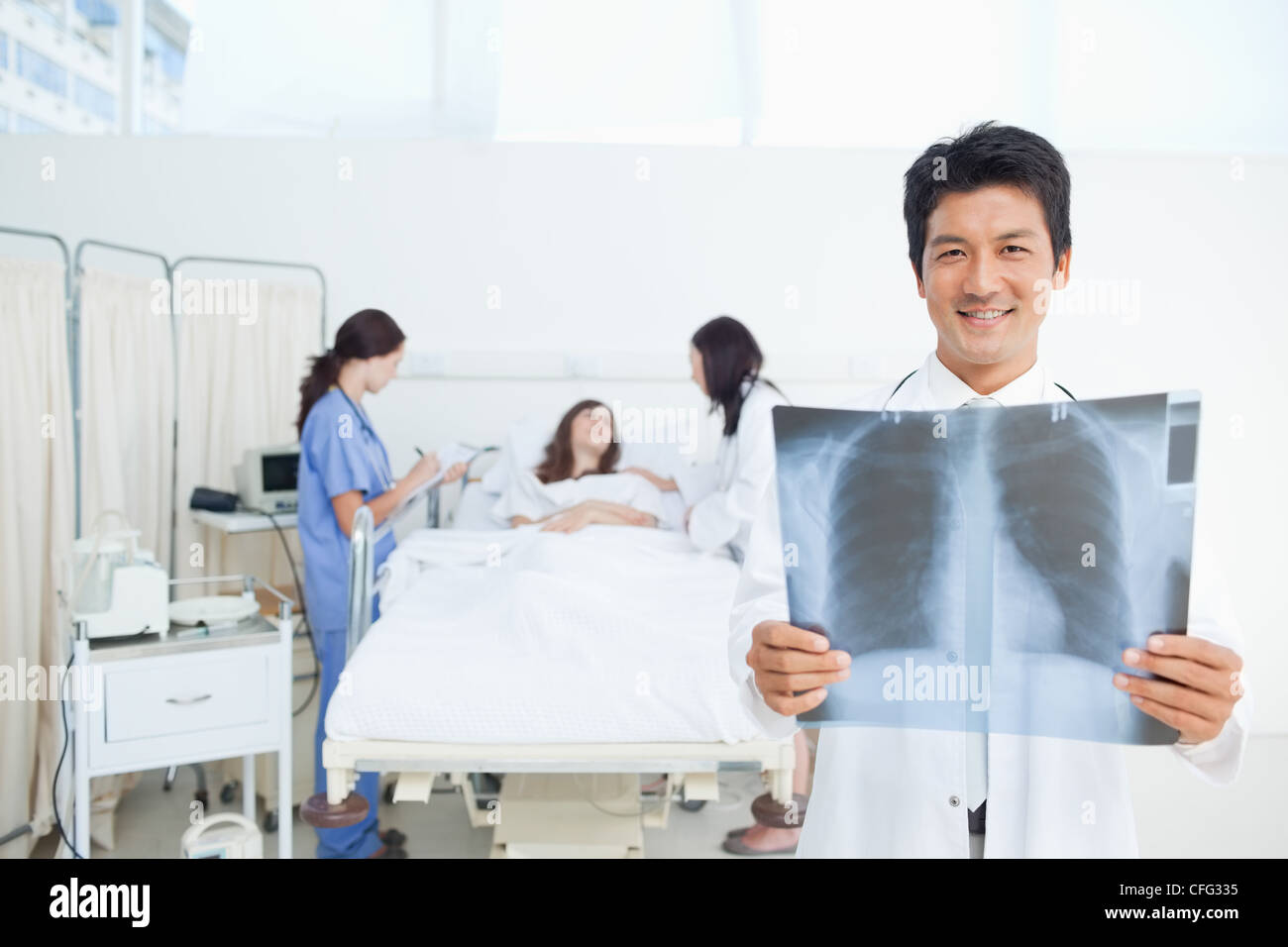 Doctor holding an x-ray scan while his colleagues are examing a patient ...