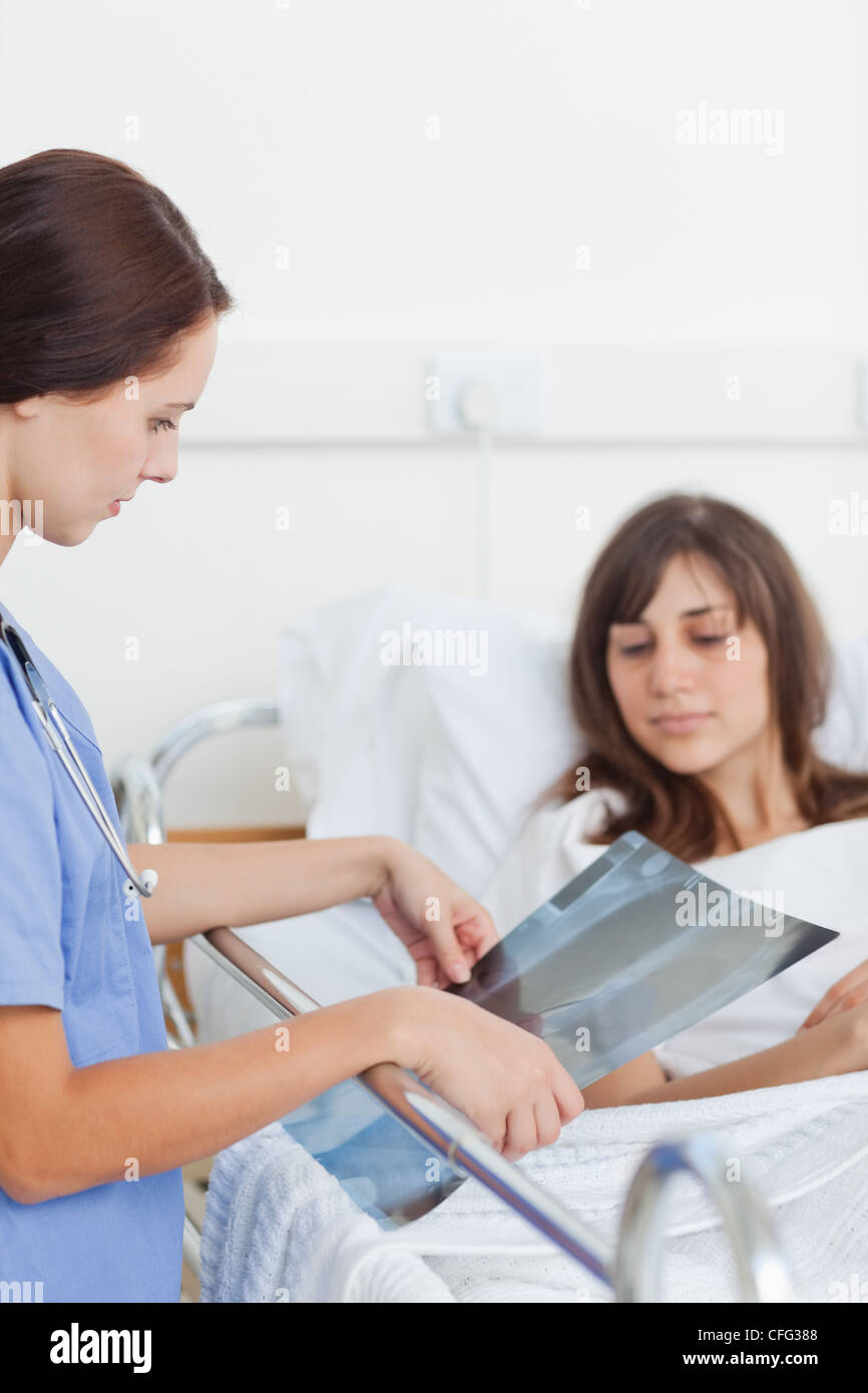 Nurse looking at an x-ray scan while standing next to a patients bed ...