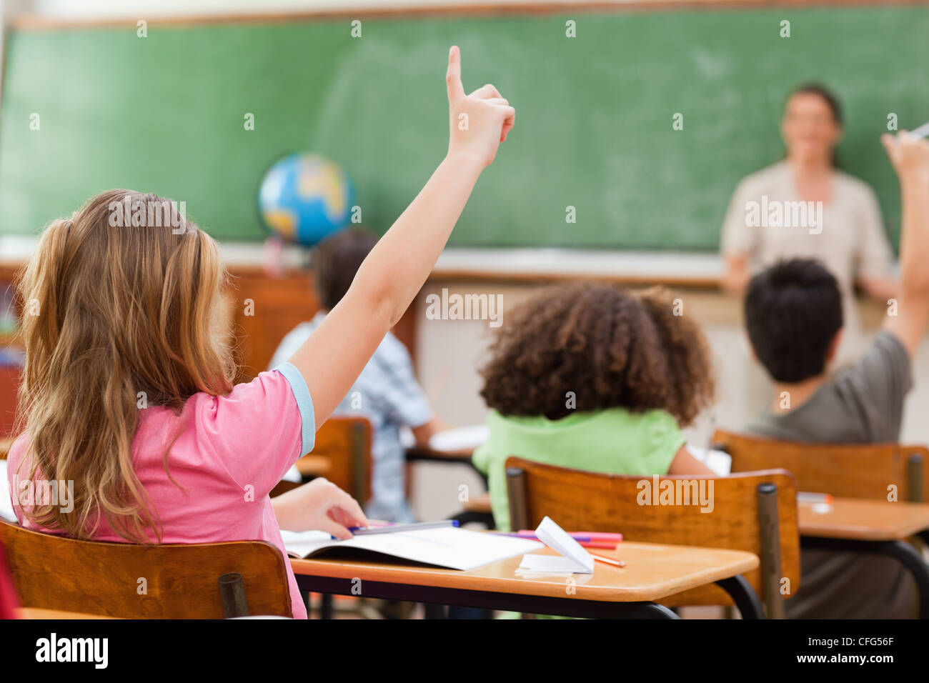 Back view of girl raising hand in class Stock Photo - Alamy