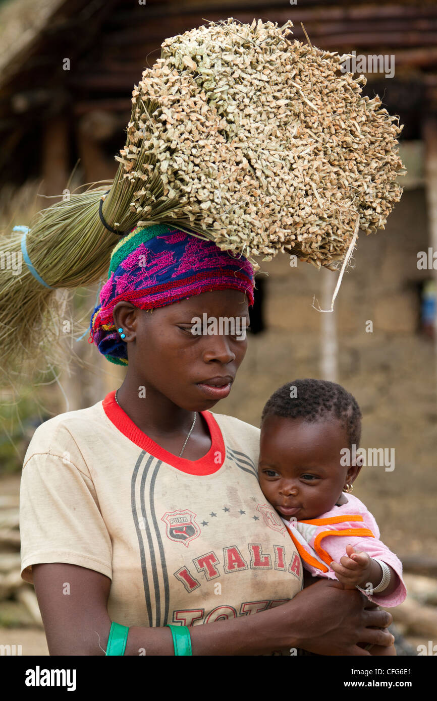A mother carrying a bundle of reed and her baby in a village near ...