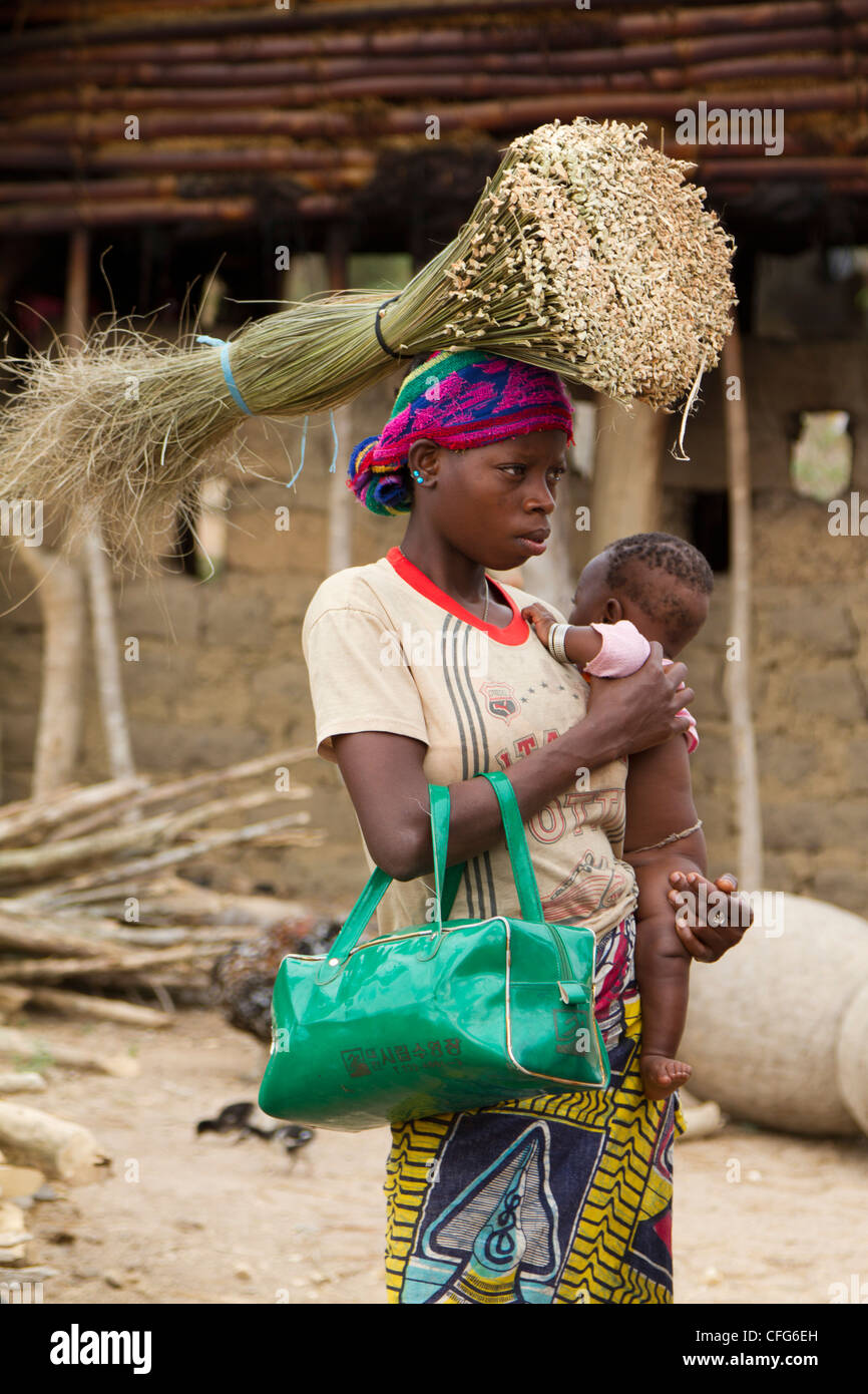 A mother carrying a bundle of reed and her baby in a village near ...