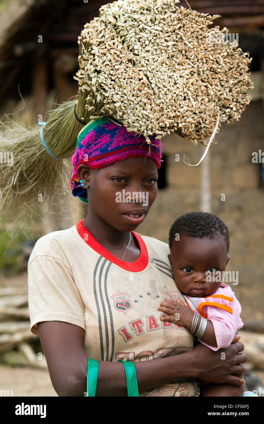 A mother carrying a bundle of reed and her baby in a village near ...