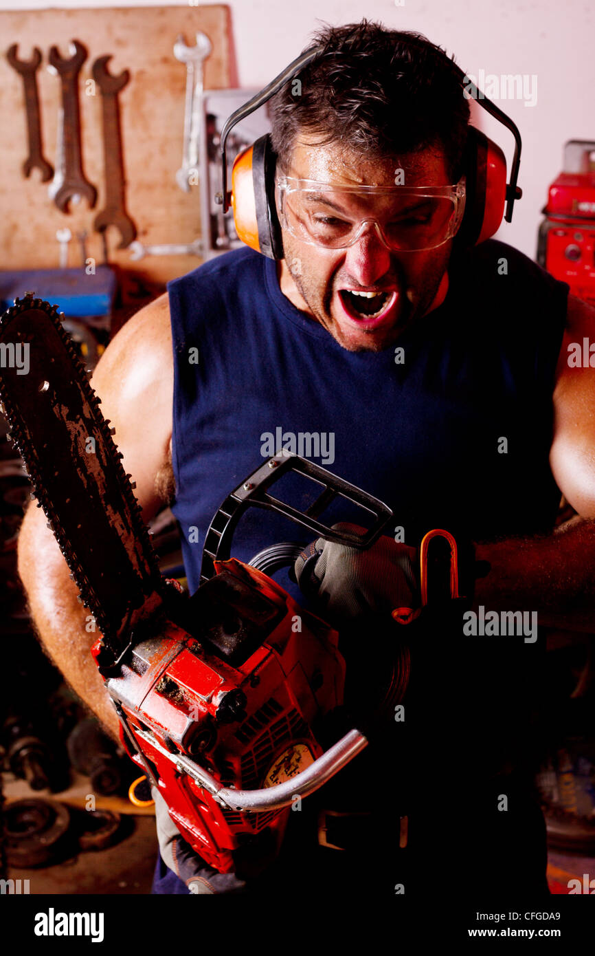 View of a angry garage mechanic man holding a chainsaw Stock Photo - Alamy