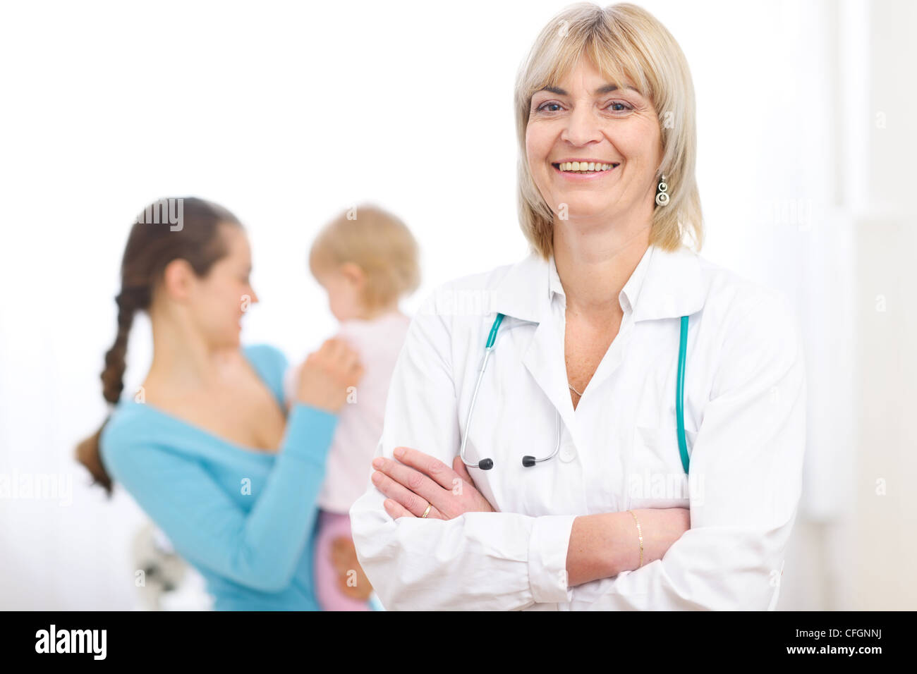 Portrait of senior pediatric doctor and mother with baby in background ...