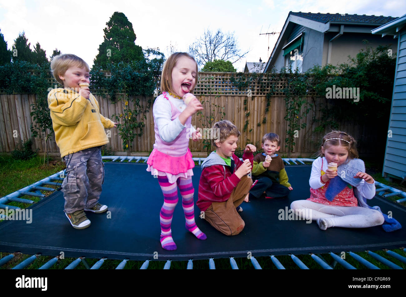 Cousins and friends playing on a trampoline whilst eating ice-cream ...